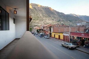Vista da rua com prédios, uma montanha ao fundo e um carro estacionado na lateral.