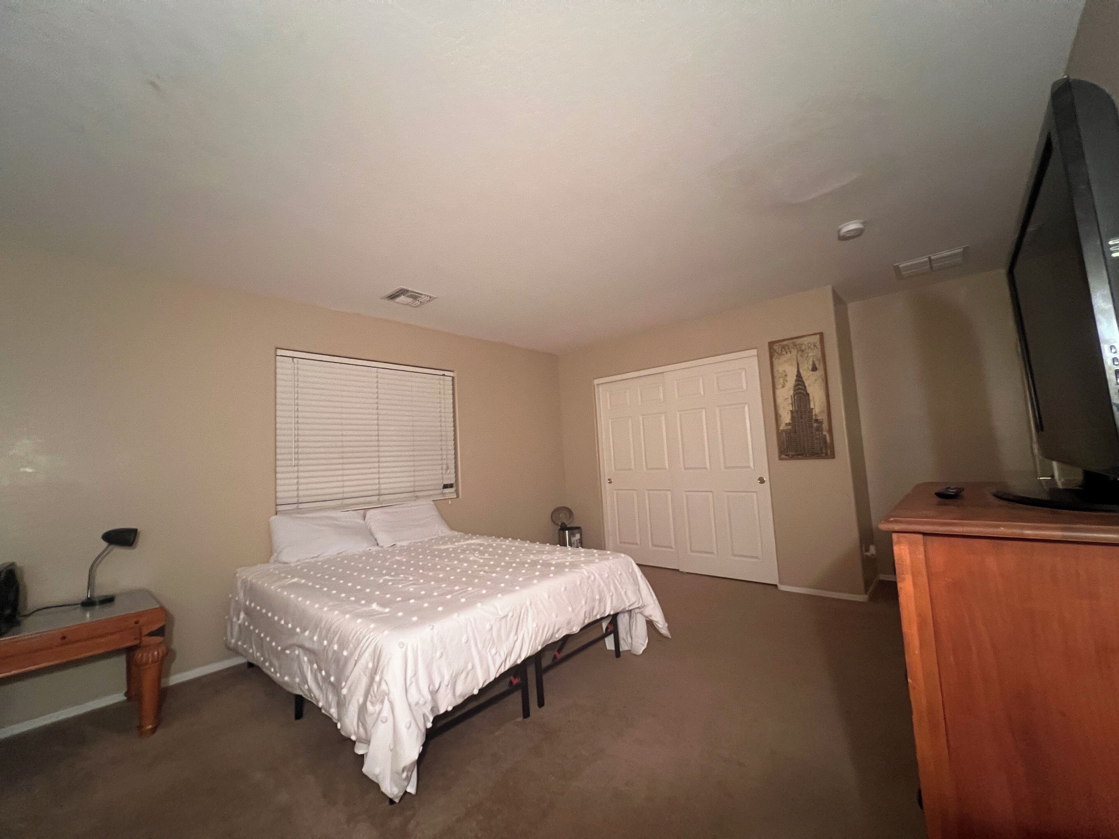 Quarto com cama, escrivaninha, televisão e porta.