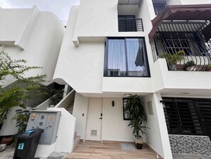 Um edifício residencial moderno de vários andares com fachada limpa, entrada visível com porta e escadaria que leva aos andares superiores.