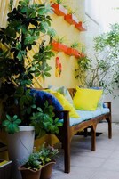Quarto com um banco de madeira, almofadas amarelas e plantas em vasos.