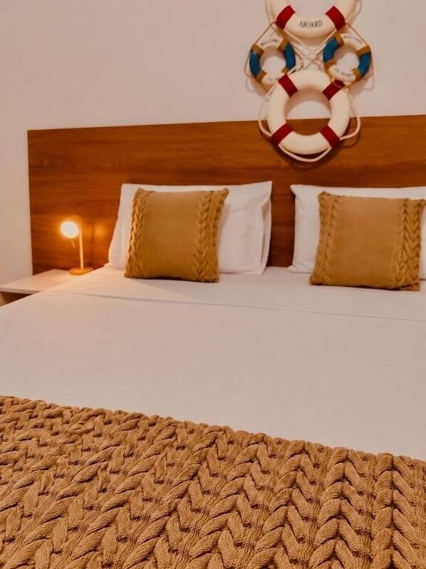 Cama com cabeceira de madeira, duas almofadas, manta de tricô e boia fixada na parede.