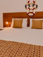 Cama com cabeceira de madeira, duas almofadas, manta de tricô e boia fixada na parede.