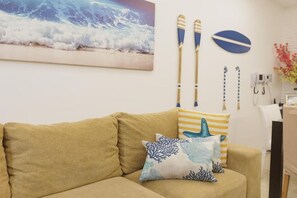 Um sofá bege com almofadas decorativas, uma pintura pendurada na parede de ondas do oceano e uma decoração com prancha de surf.