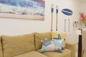 Um sofá bege com almofadas decorativas, uma pintura pendurada na parede de ondas do oceano e uma decoração com prancha de surf.