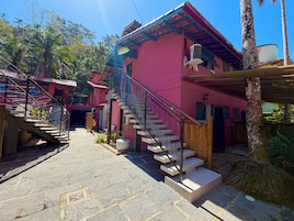 Edifício rosa com escadaria que dá para um segundo andar, cercado por vegetação e céu claro.