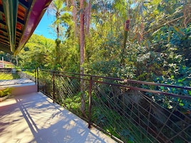 Varanda com guarda-corrimão de metal, vista para um jardim exuberante com diversas plantas e árvores.