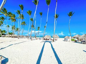 Uma praia com palmeiras, cabanas de palha e um céu azul límpido.