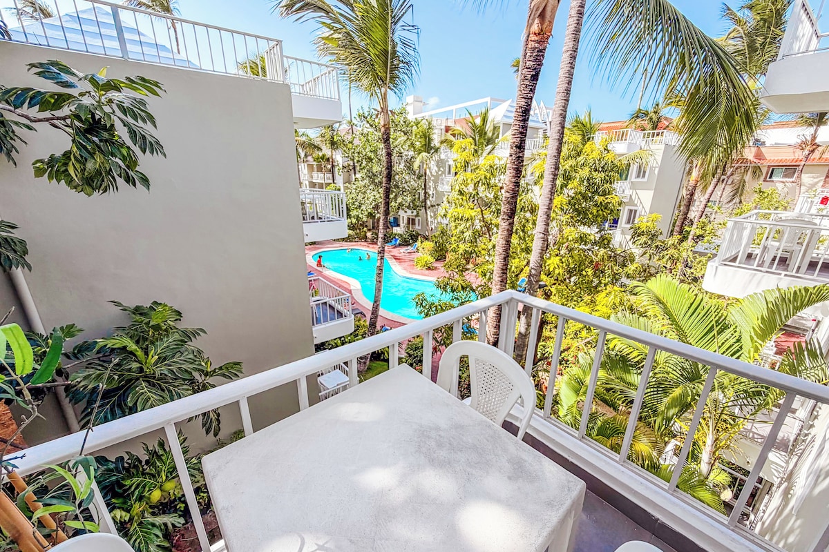 Varanda com vista para uma piscina, cercada por palmeiras e vegetação.