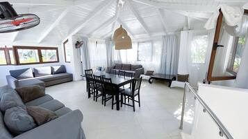 Uma sala de estar ampla com teto alto, uma mesa de jantar rodeada por cadeiras e um sofá.