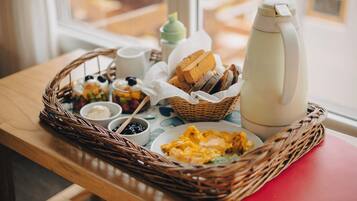 Bandeja de café da manhã com ovos, torradas, frutas e café sobre uma mesa de madeira perto de uma janela.