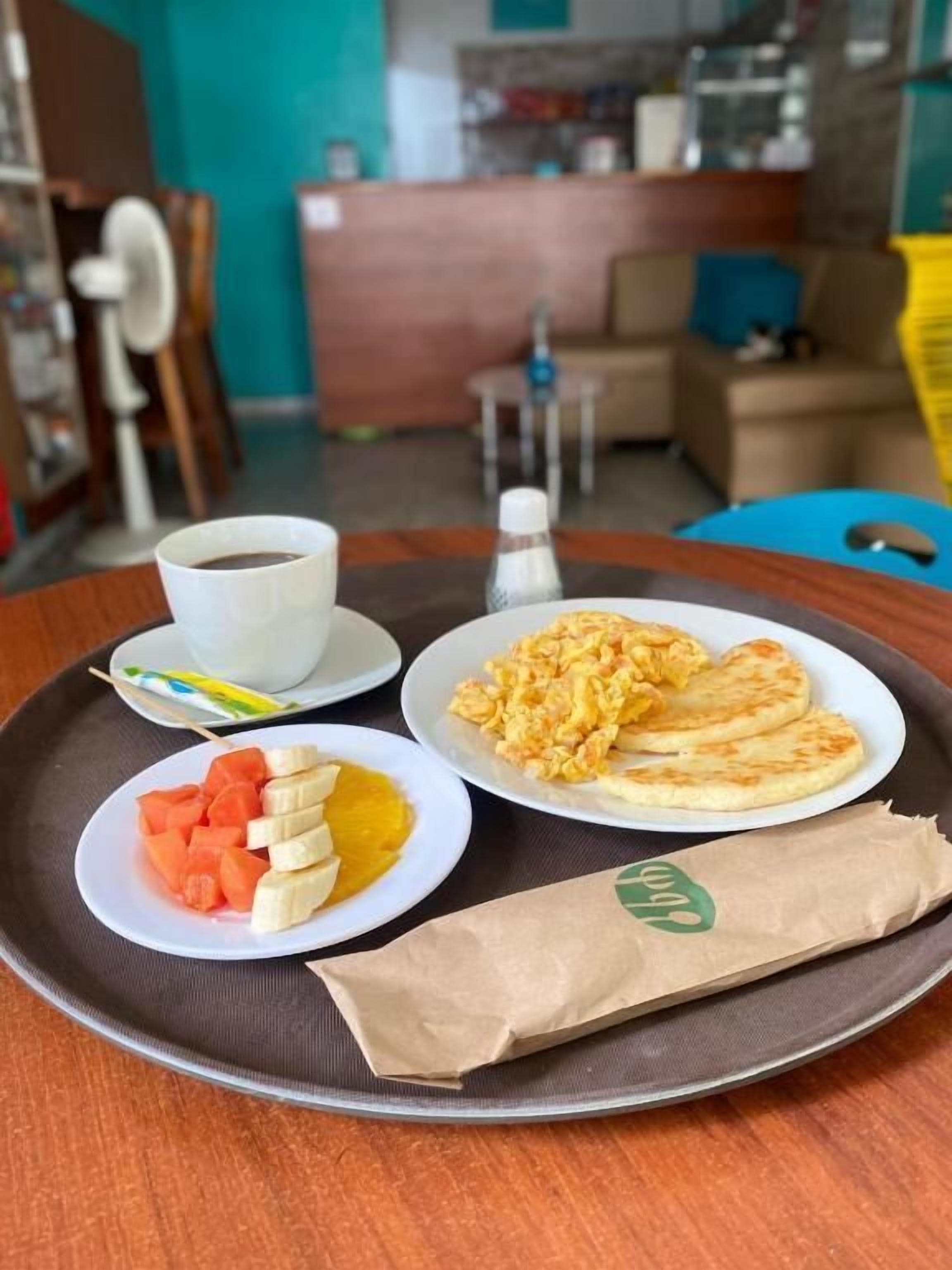 Uma bandeja com xícara de café, ovos mexidos e frutas sobre uma mesa de madeira.