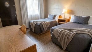 Quarto de hotel com duas camas, uma escrivaninha de madeira, um criado-mudo com abajur e uma porta com a numeração 403.