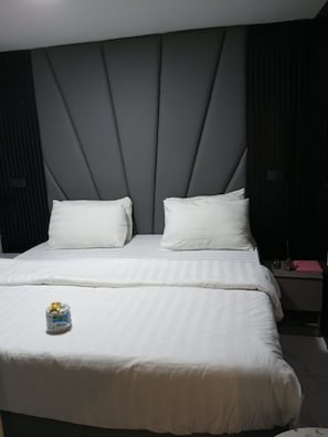 Quarto de hotel com uma cama grande, cabeceira e mesa de cabeceira com abajur e telefone.
