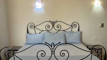 Cama com estrutura de metal e colchão branco, duas luzes fixadas na parede e ar condicionado na parede.