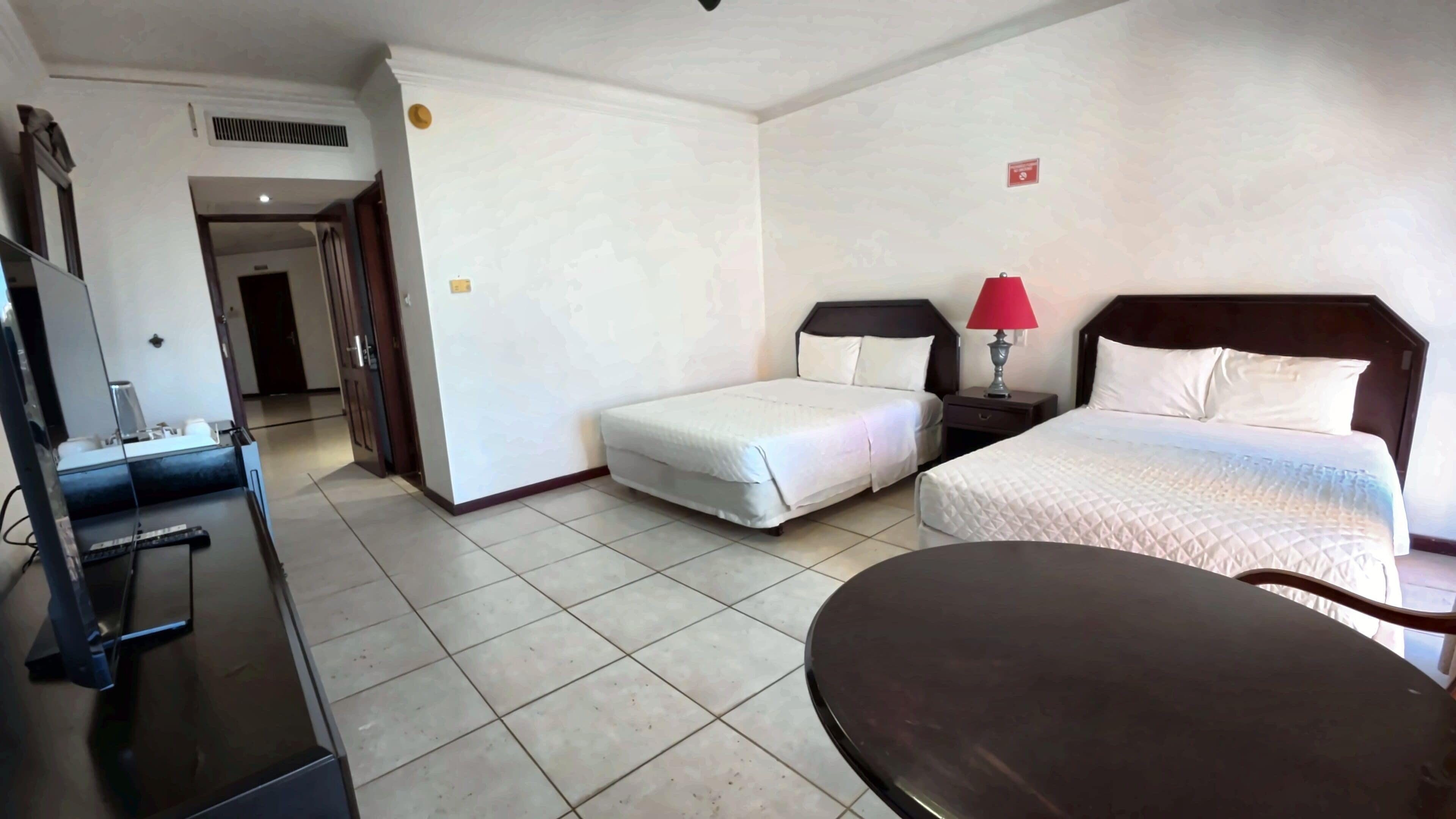 Quarto de hotel com cama, mesas de cabeceira, escrivaninha e uma cadeira, e televisão.