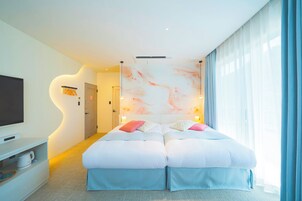 Quarto de hotel moderno com uma cama grande, televisão de tela plana e parede com padrão marmorizado.