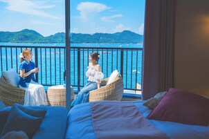 Varanda com mobiliário de vime, cama com almofadas e vista para o mar e montanhas.