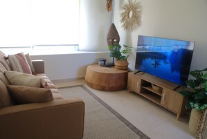 Uma sala de estar com um sofá, uma televisão, uma mesinha de madeira e uma janela.