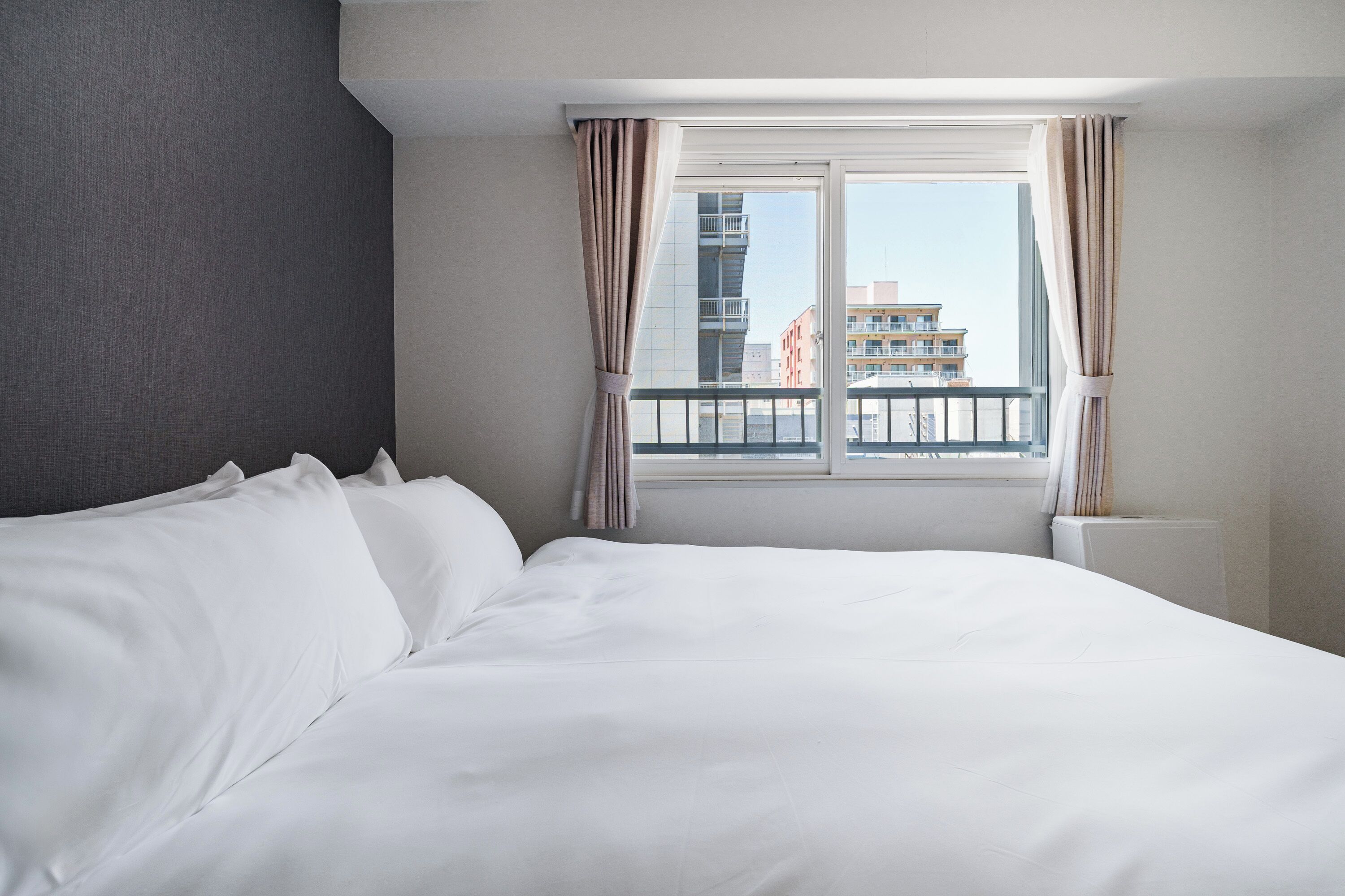 Quarto de hotel com uma cama grande, uma janela com cortinas e vista para edifícios.