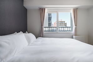 Quarto de hotel com uma cama grande, uma janela com cortinas e vista para edifícios.