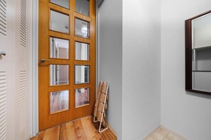 Uma porta de madeira com vários painéis de vidro, uma parede branca com acabamento texturizado e um chão de madeira.