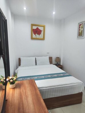 Quarto com cama, mesa de cabeceira, abajur e duas fotos emolduradas na parede.