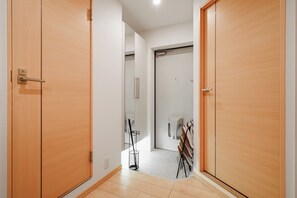 Corredor com portas de madeira, chão de azulejos e um cabideiro com chapéus.