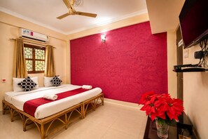 Quarto de hotel com cama, ventoinha no teto, ar condicionado, parede texturizada vermelha e planta em vaso.