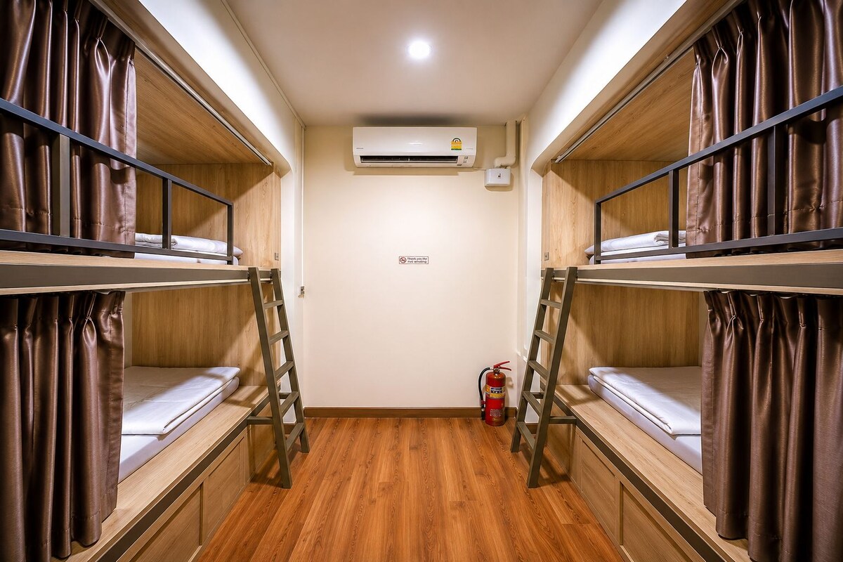 Quarto com beliches, ar condicionado, extintor de incêndio e piso de madeira.