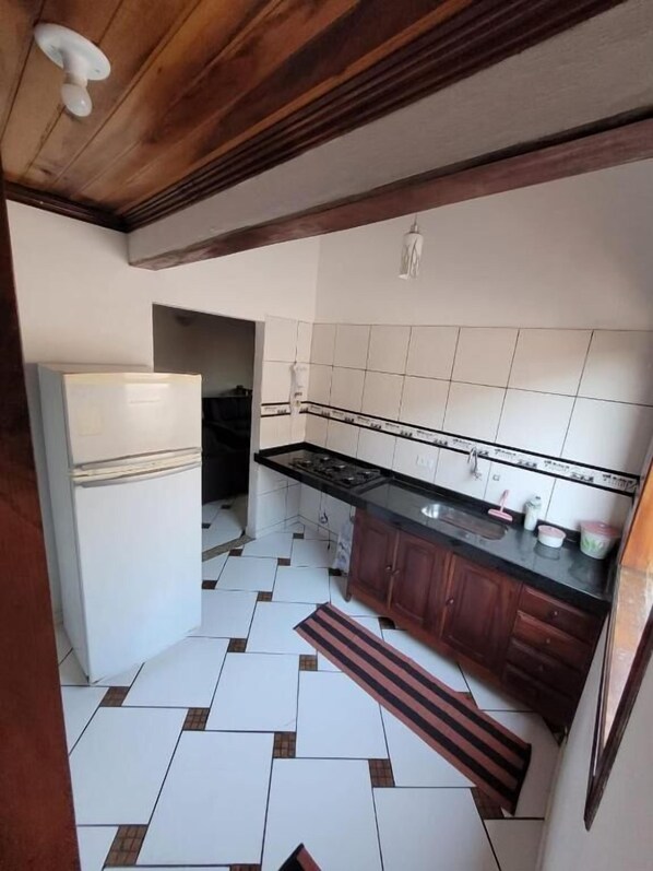 Cozinha com piso em azulejos brancos e castanhos, armários de madeira, bancada preta e geladeira branca.
