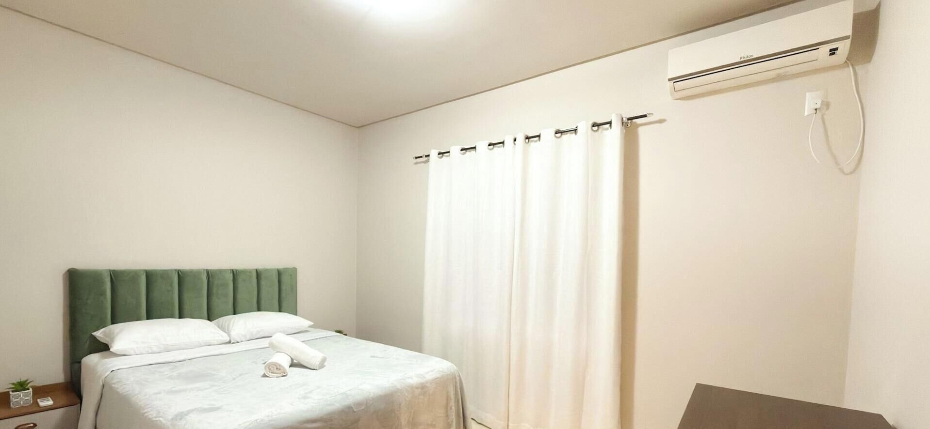 Quarto de hotel com cama, mesa de cabeceira, ar condicionado fixado na parede e cortina.