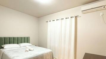 Quarto de hotel com cama, mesa de cabeceira, ar condicionado fixado na parede e cortina.