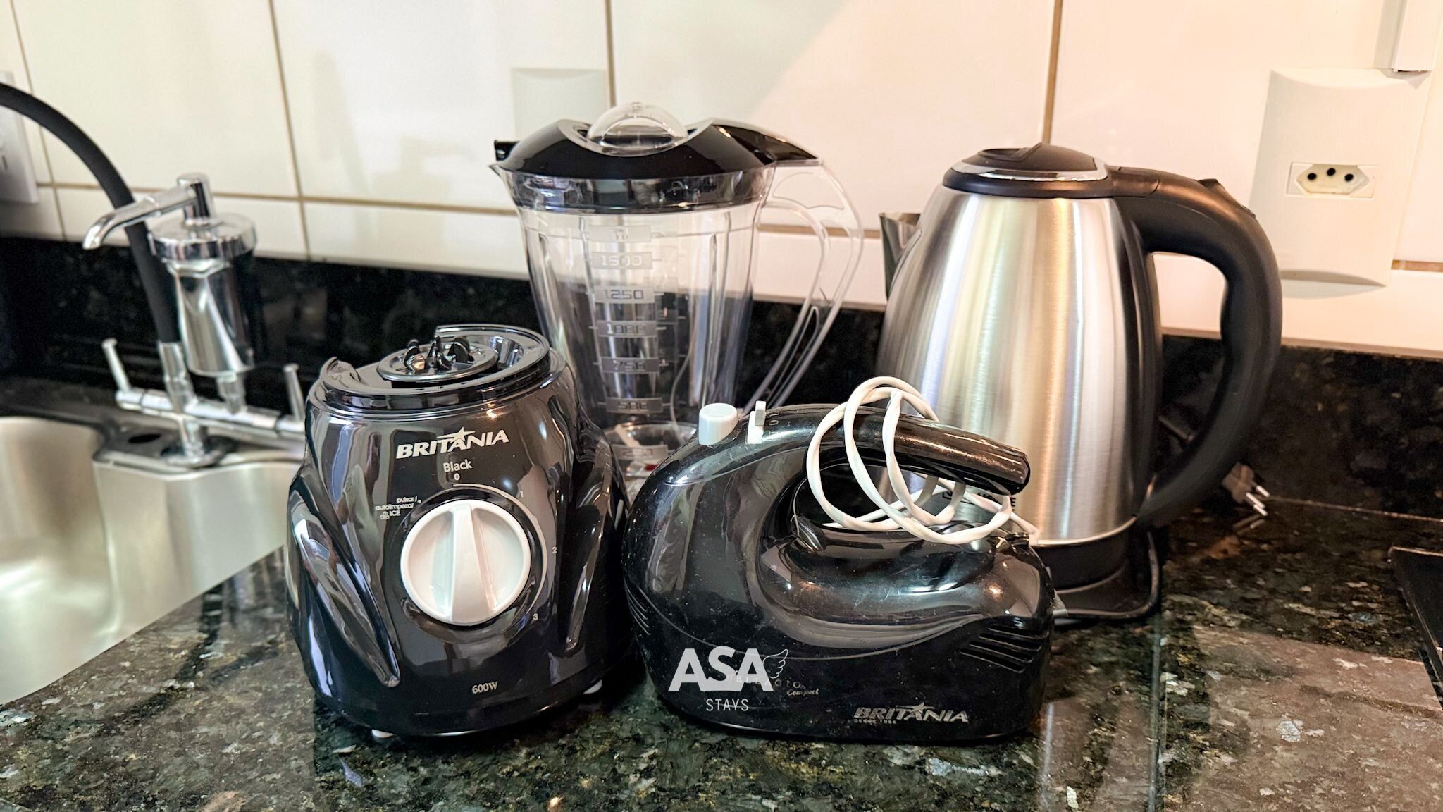 Uma bancada de cozinha com liquidificador, chaleira e cafeteira.