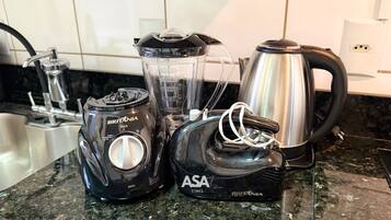 Uma bancada de cozinha com liquidificador, chaleira e cafeteira.