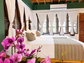 Quarto com duas camas, janela com cortinas, ar-condicionado e teto de madeira.