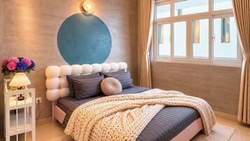 Quarto com cama, luminária de cabeceira, um vaso com flores e janela com cortinas.