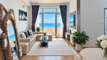 Sala de estar moderna com sofá, mesa de centro e vista para o mar através de grandes janelas.