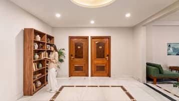 Um interior moderno com estante de madeira, portas duplas, sofá verde e piso de mármore.