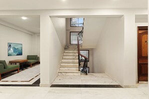 Interior moderno com escadaria de mármore, sofá verde e porta de madeira.