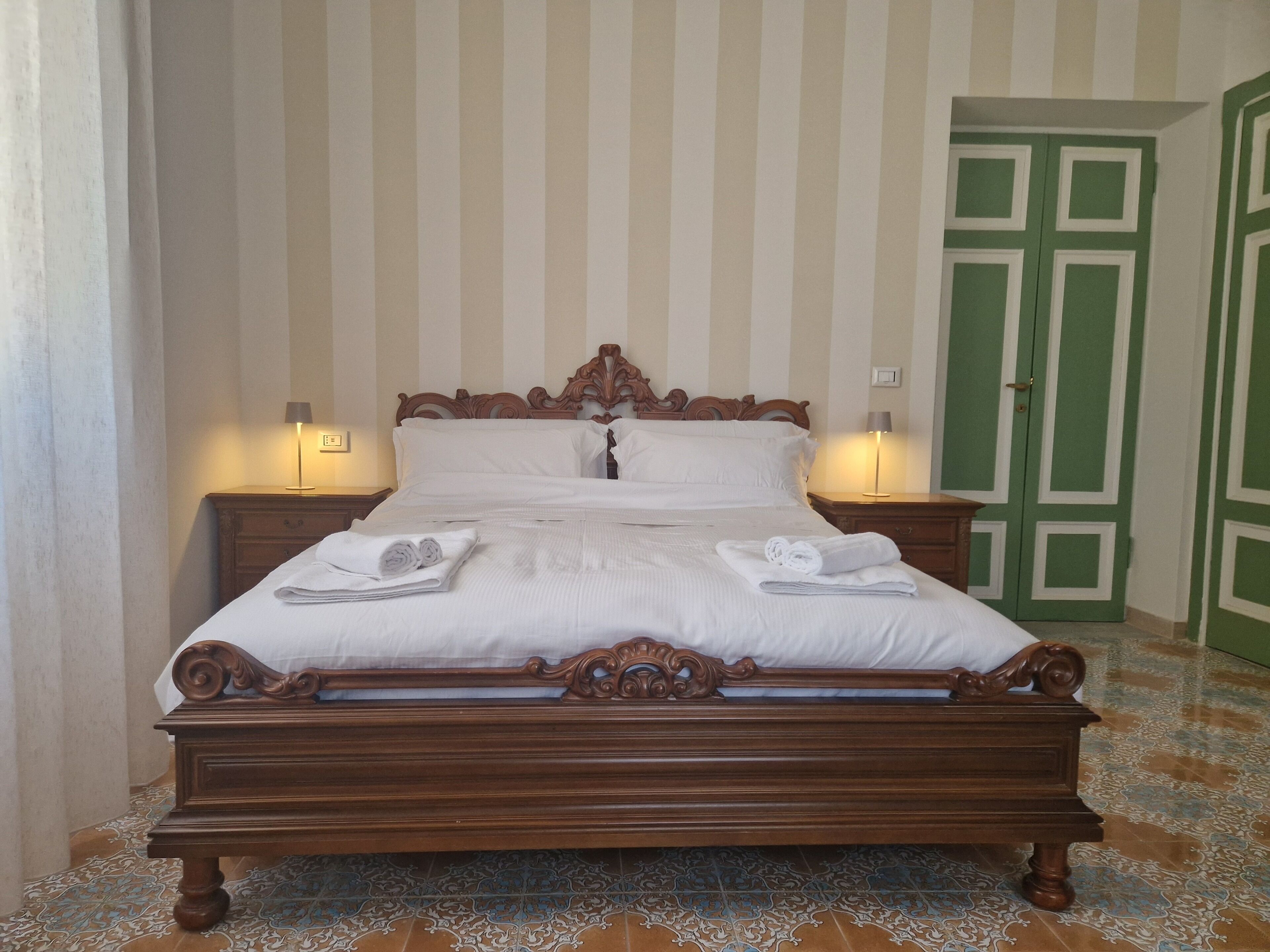 Cama bem arrumada com almofadas e toalhas, duas luminárias de cabeceira e uma porta verde ao fundo.