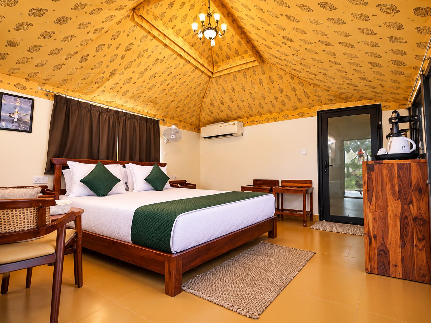 Quarto com cama, escrivaninha, cadeira, ventilador e cafeteira.