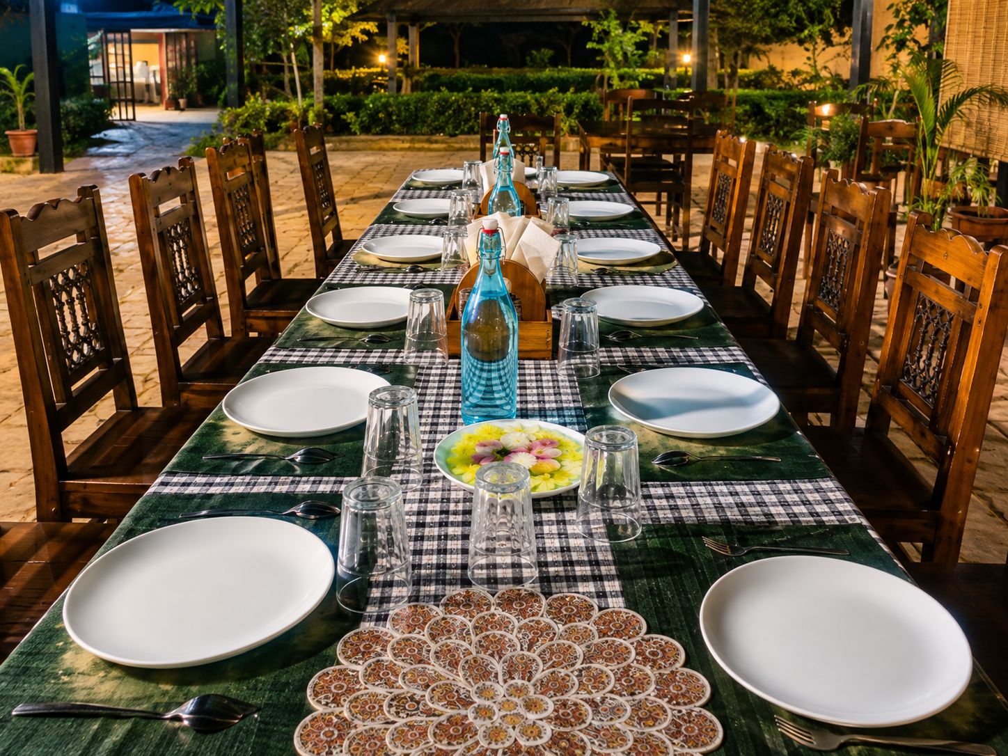 Mesa de jantar posta para uma refeição, com cadeiras, pratos, talheres e uma garrafa de água.