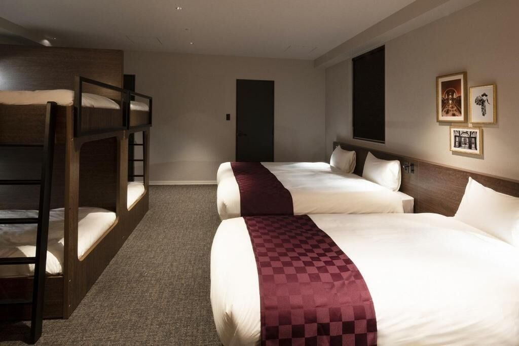 Quarto de hotel com beliches, uma cama grande e manta xadrez.
