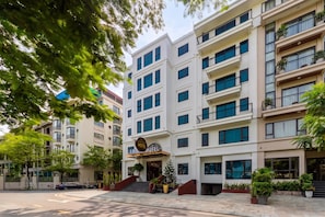 Um hotel com vários andares, uma entrada destacada, uma escadaria que leva à entrada principal e uma área de estacionamento em frente.
