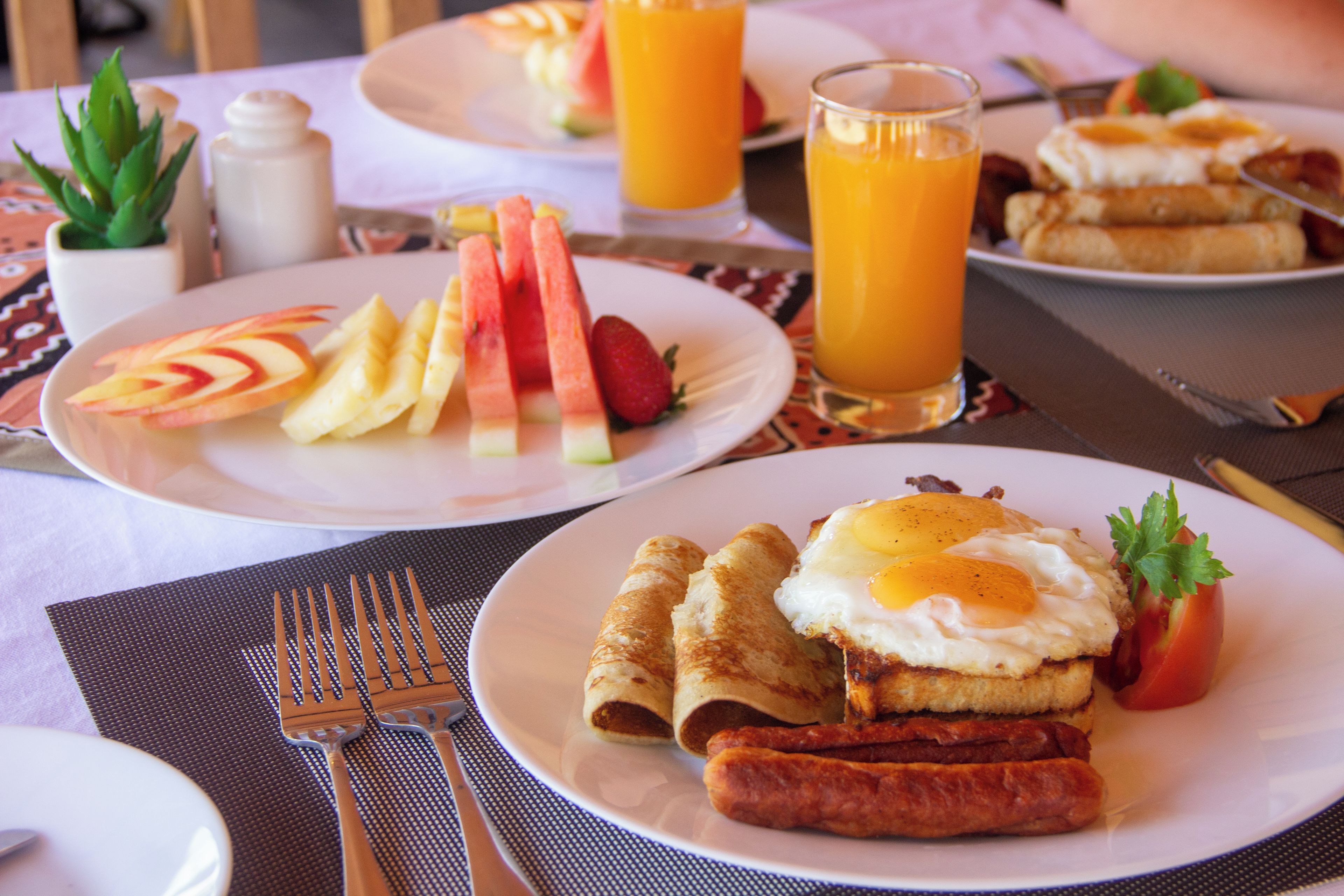 Uma mesa posta para o café da manhã, com pratos de comida, um copo de suco de laranja e um garfo.