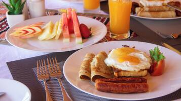 Uma mesa posta para o café da manhã, com pratos de comida, um copo de suco de laranja e um garfo.