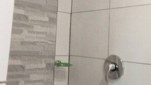 Casa de banho com zona de duche, parede revestida em azulejos e chuveiro no canto.