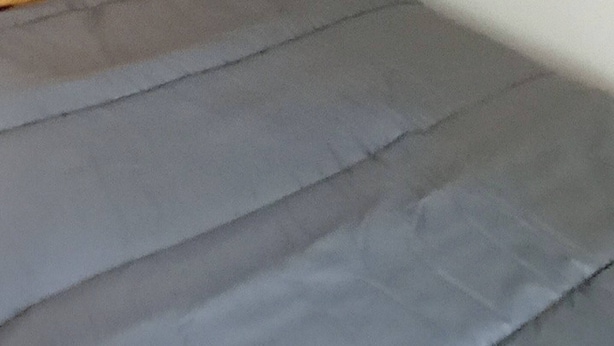 Cama com roupa de cama cinza e dois travesseiros, um amarelo e um cinza.