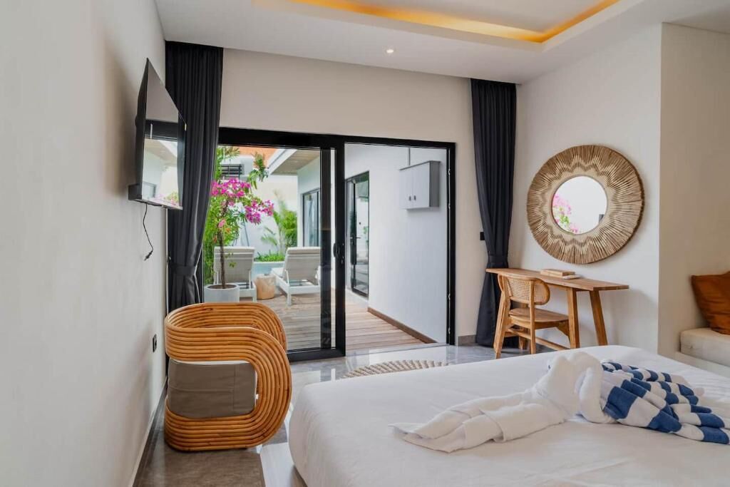 Quarto de hotel com cama, escrivaninha, cadeira, televisão e vista para área externa com mesa e cadeiras.