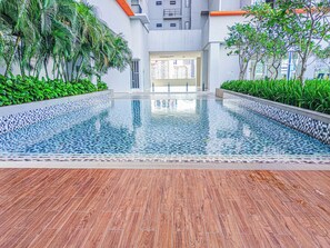 Piscina com borda em azulejo, cercada por vegetação e um deck de madeira.